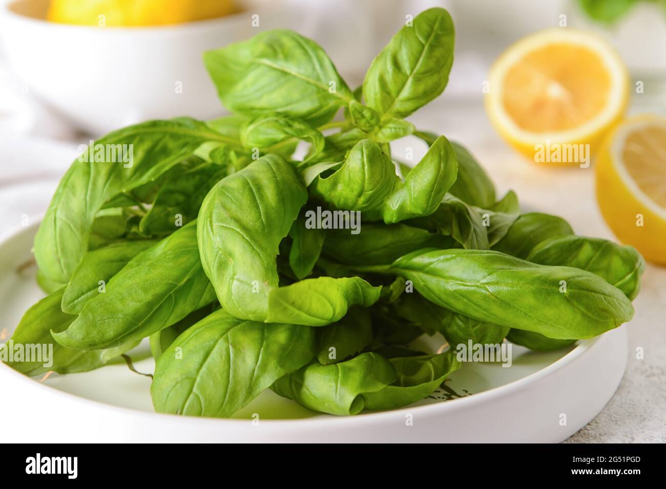 Tray with fresh basil leaves and lemons on light background, closeup ...