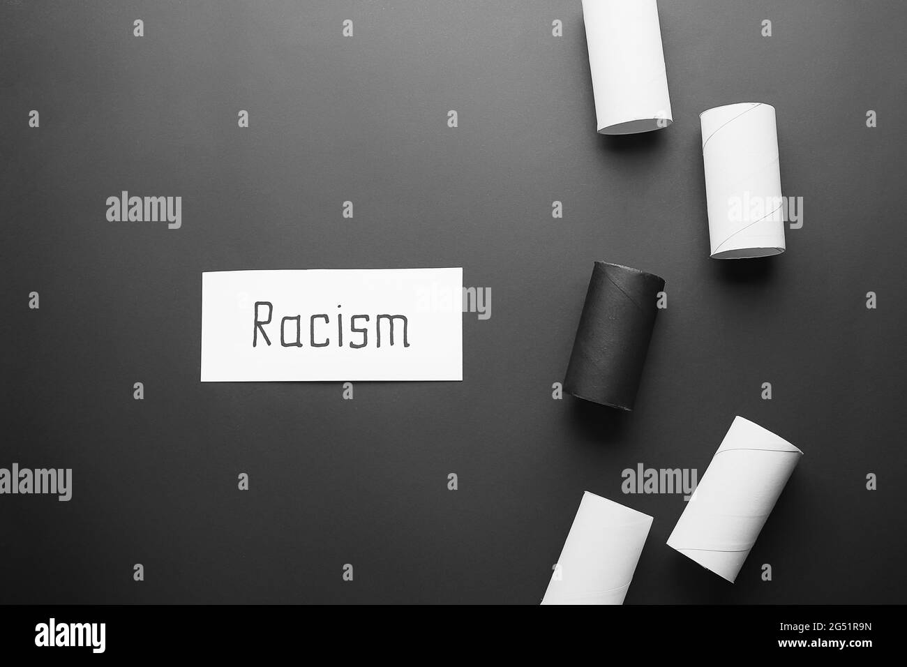 Paper piece with word RACISM and cardboard tubes on dark background ...