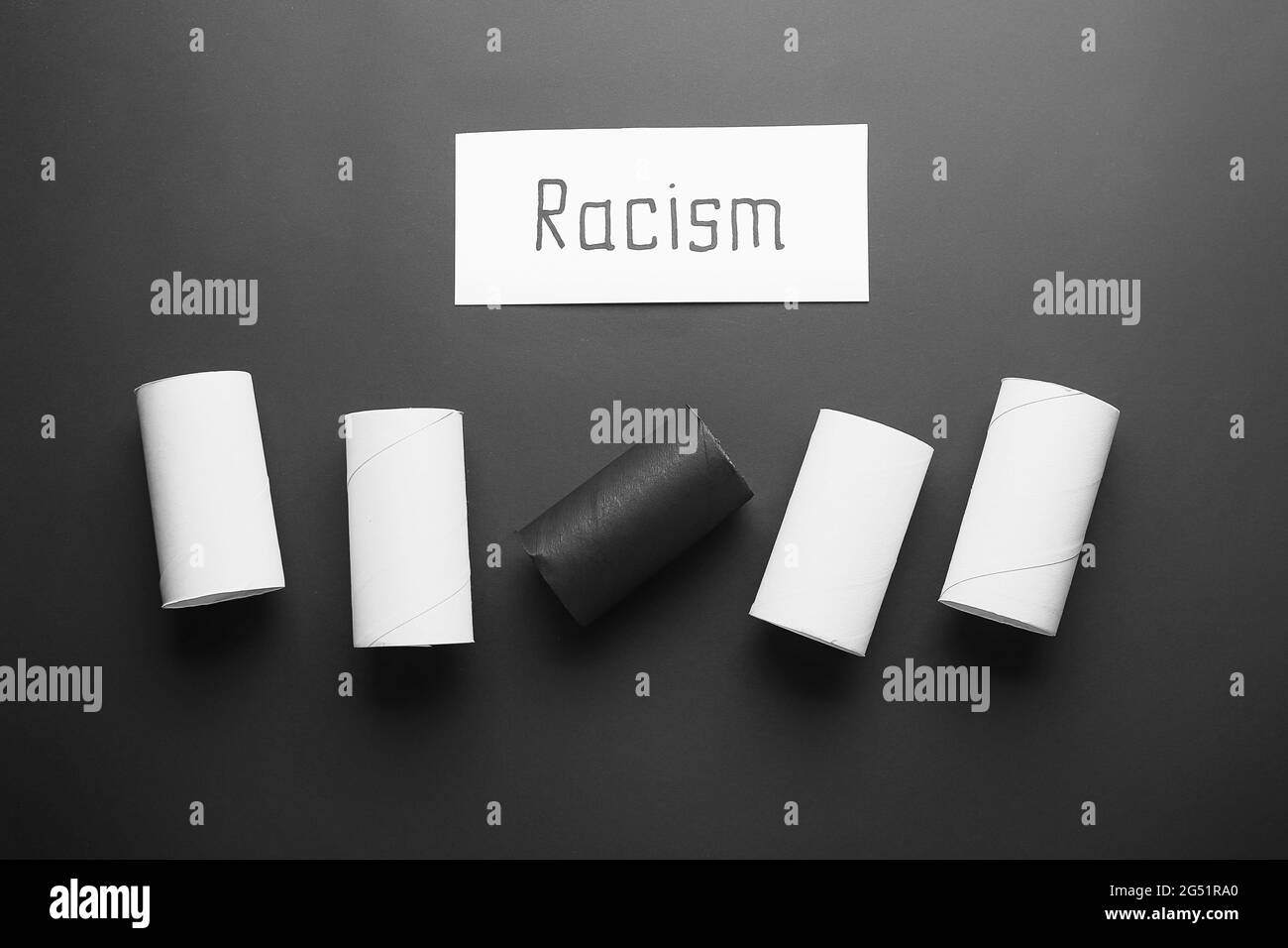 Paper piece with word RACISM and cardboard tubes on dark background ...