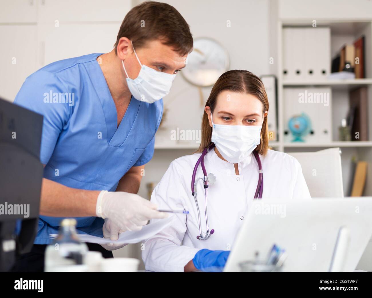 Doctor and nurse in protective mask check patient data in hospital ...