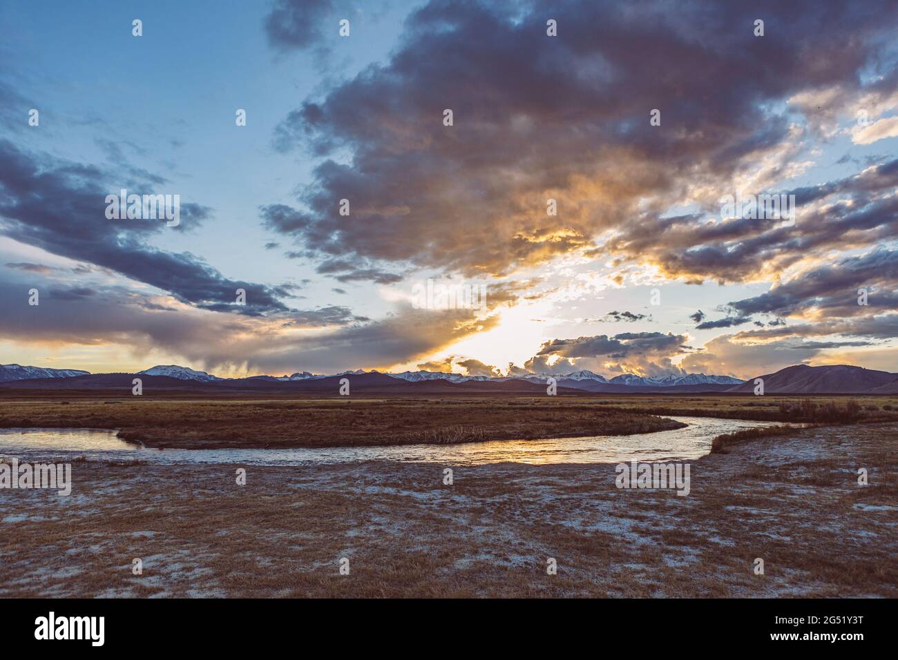 River runs though Arid plain against Dramatic sunset sky and Mountains ...