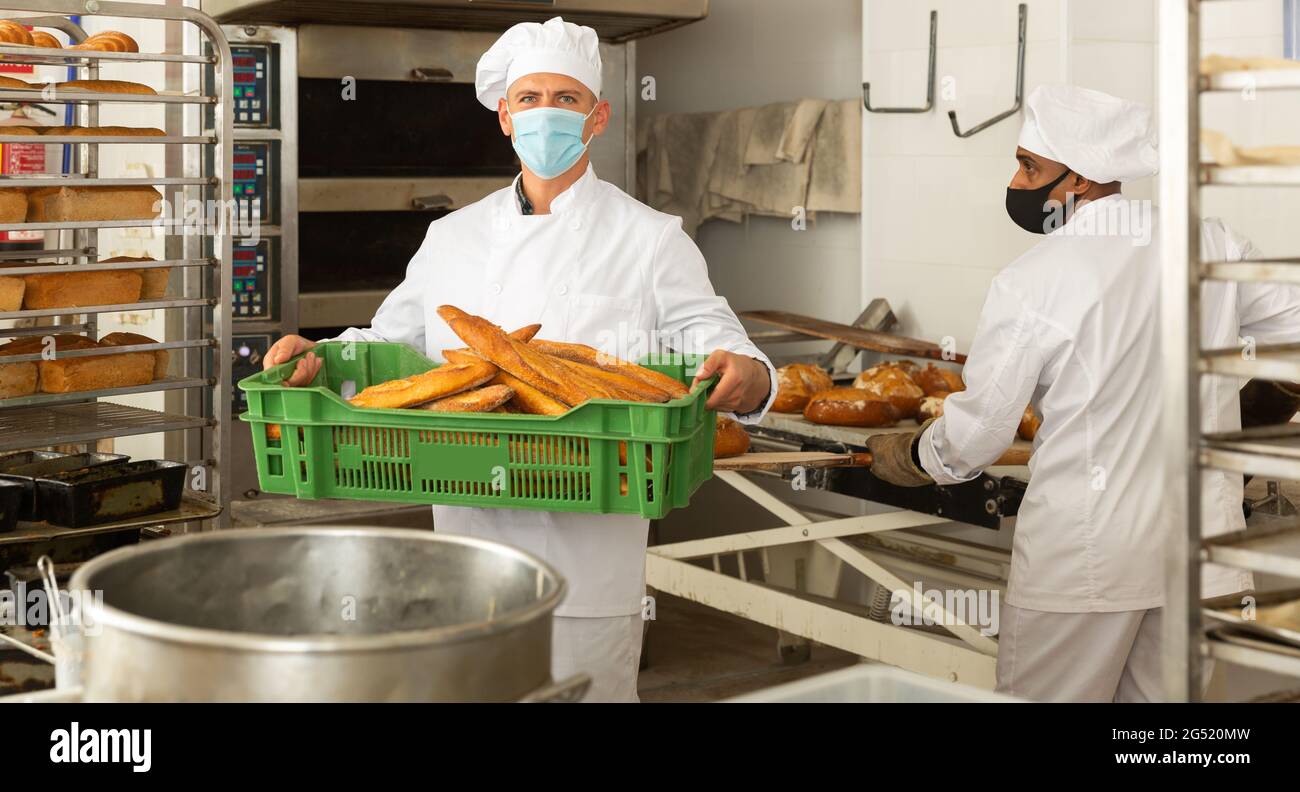 Baker in mask carrying crate with bread Stock Photo - Alamy