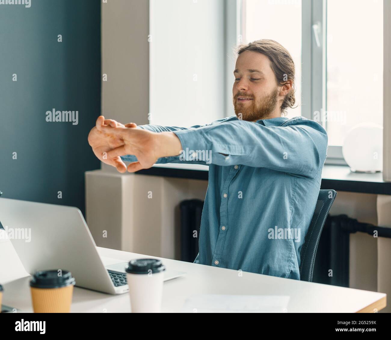 Young tired man office worker in casual clothes stretching arms at ...
