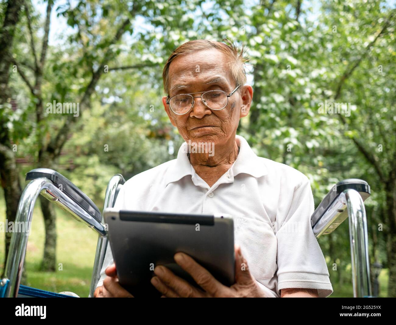 Senior man in wheelchair using digital tablet, looking at screen ...