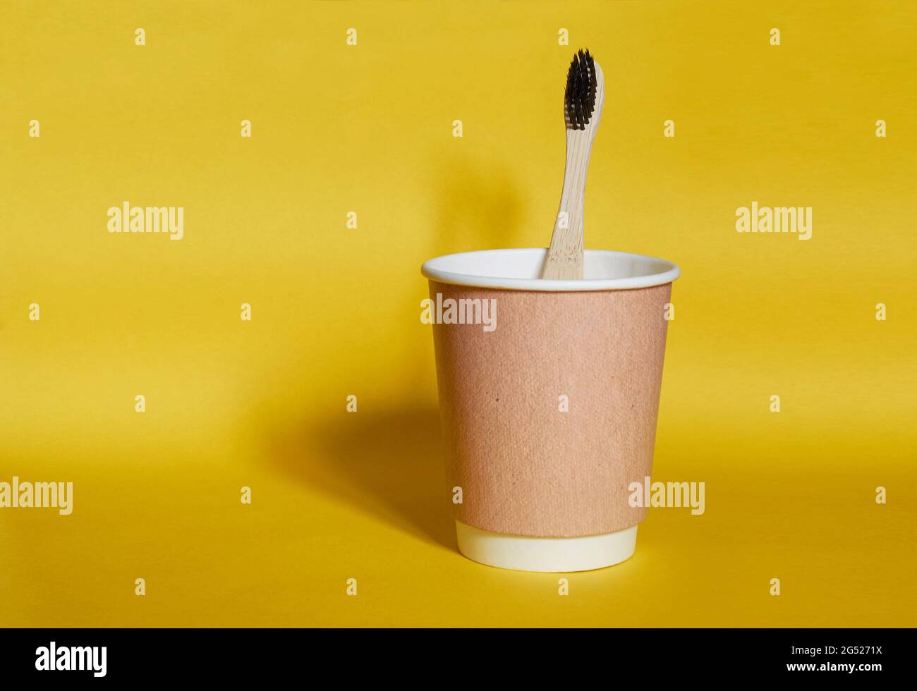 Wooden toothbrush in a cardboard cup on a yellow background. Horizontal ...