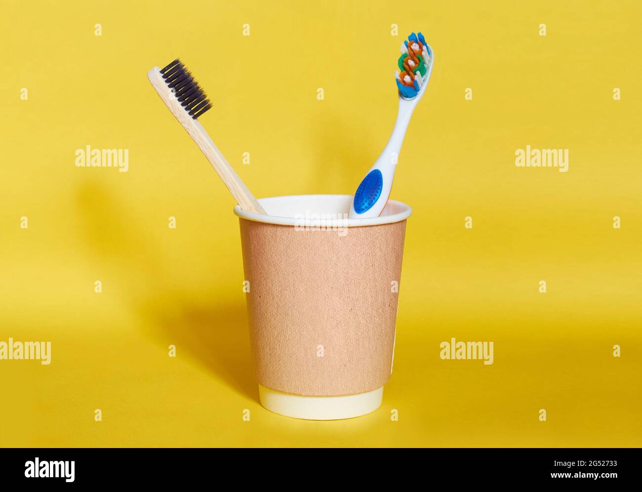 Wooden and plastic toothbrushes in a cardboard cup on a yellow ...