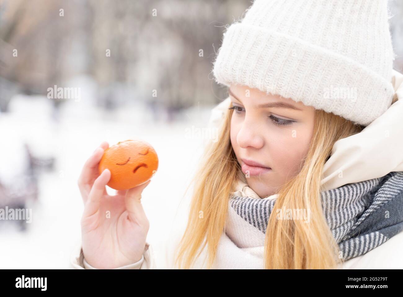 young beautiful woman is sad in winter. holding a tangerine in his hand ...