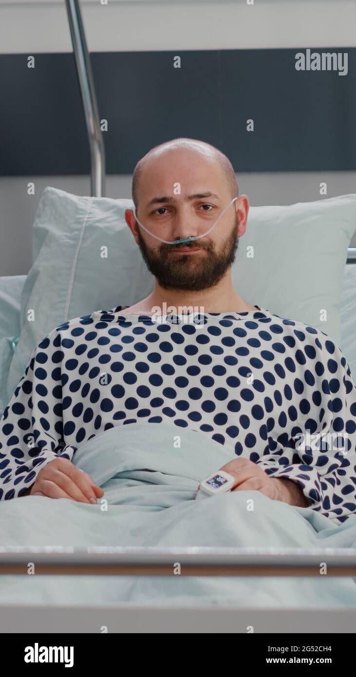 Potrait of sad sick man wearing nasal oxygen tube lying in bad looking ...