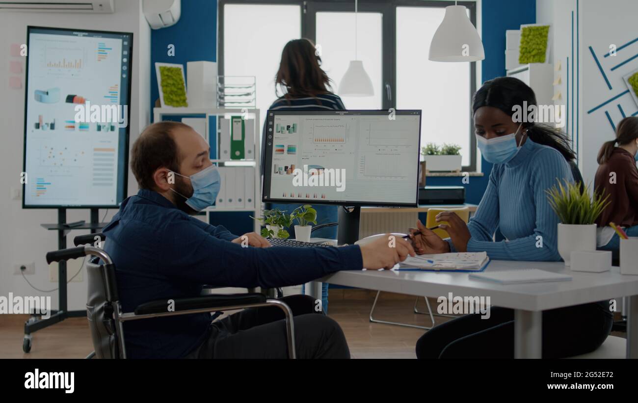 Diverse colleagues with masks respecting social distance working with ...