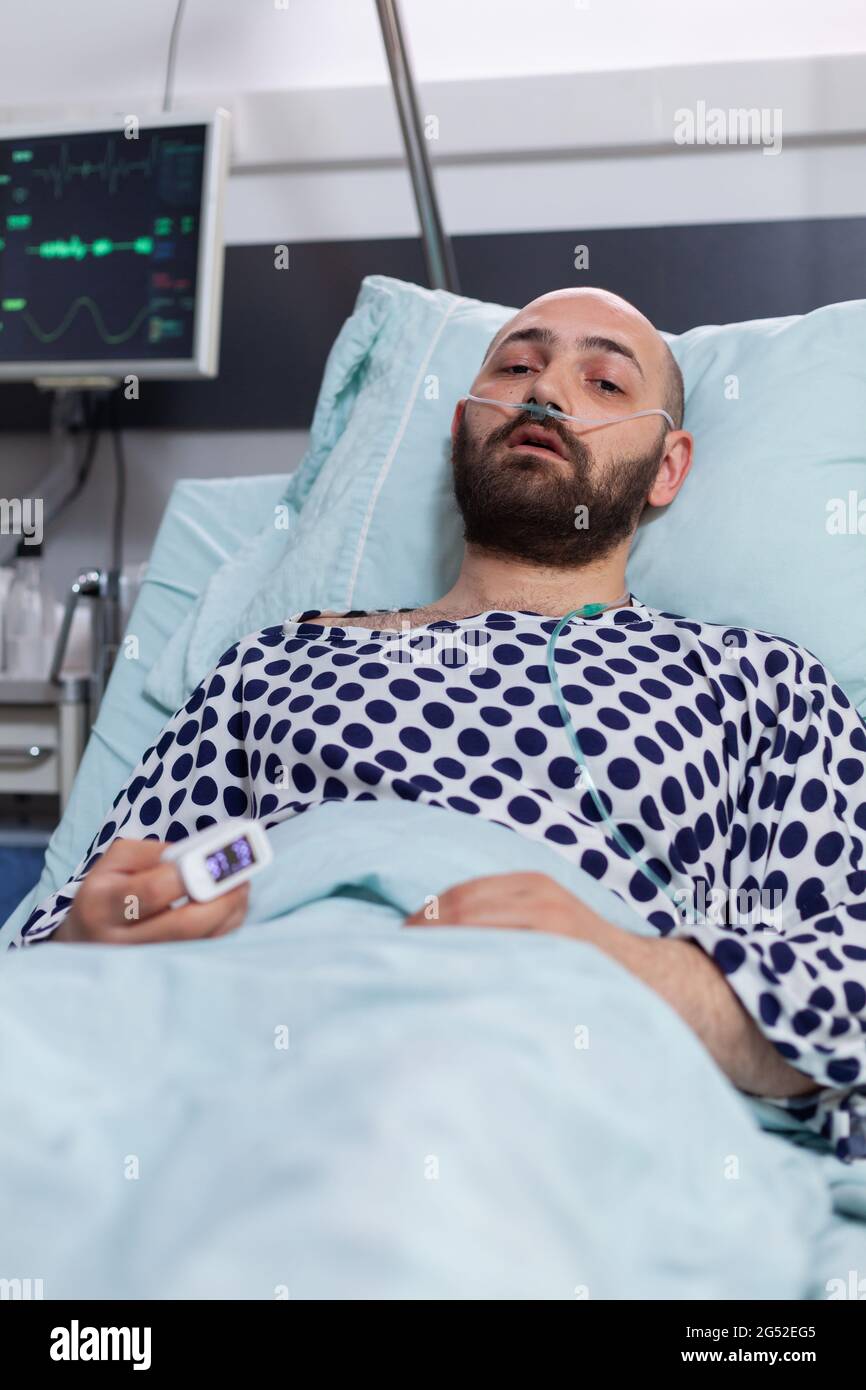 Sad sick man with nasal oxygen tube resting in bad looking into camera ...