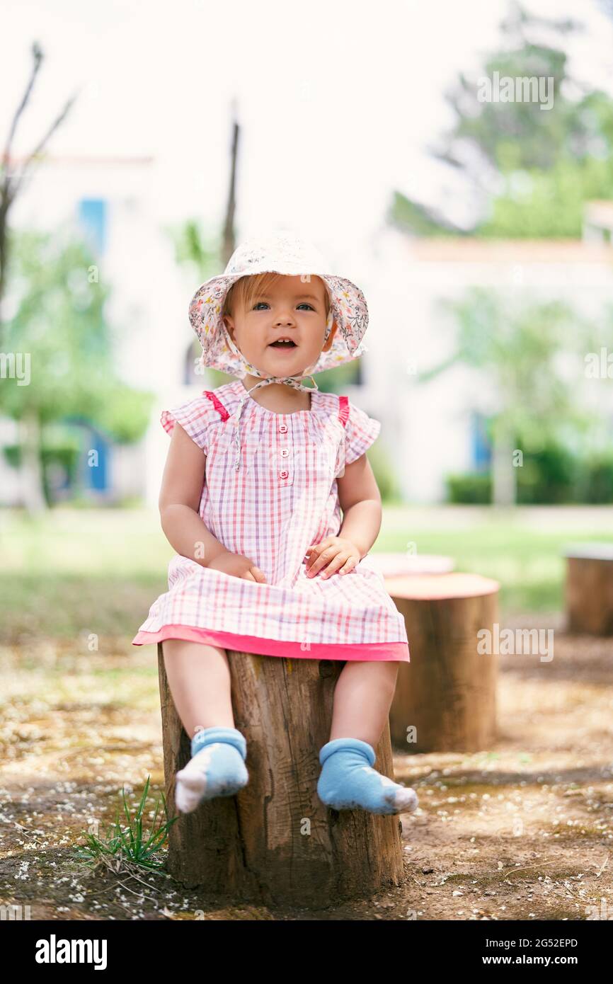 Little girl in a hat sits on a tree stump Stock Photo - Alamy