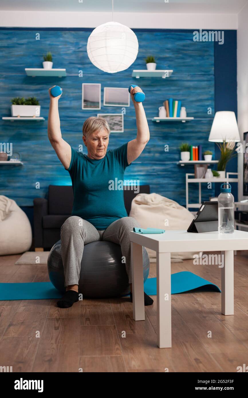 Senior woman in retirement raising hands doing arms exercise using ...