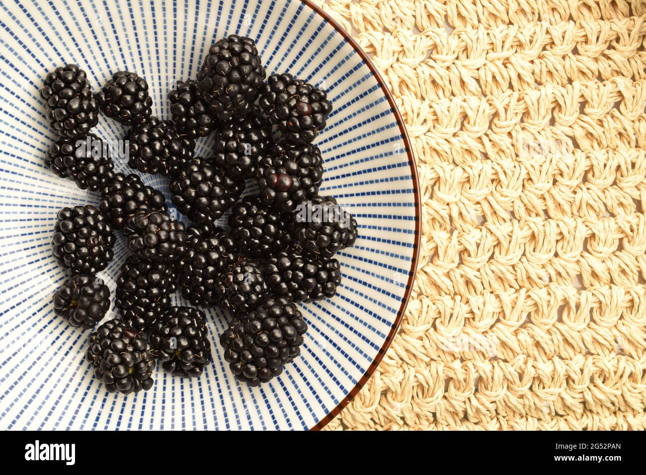 Ripe blackberries in a ceramic plate, close-up, on a straw mat, top ...