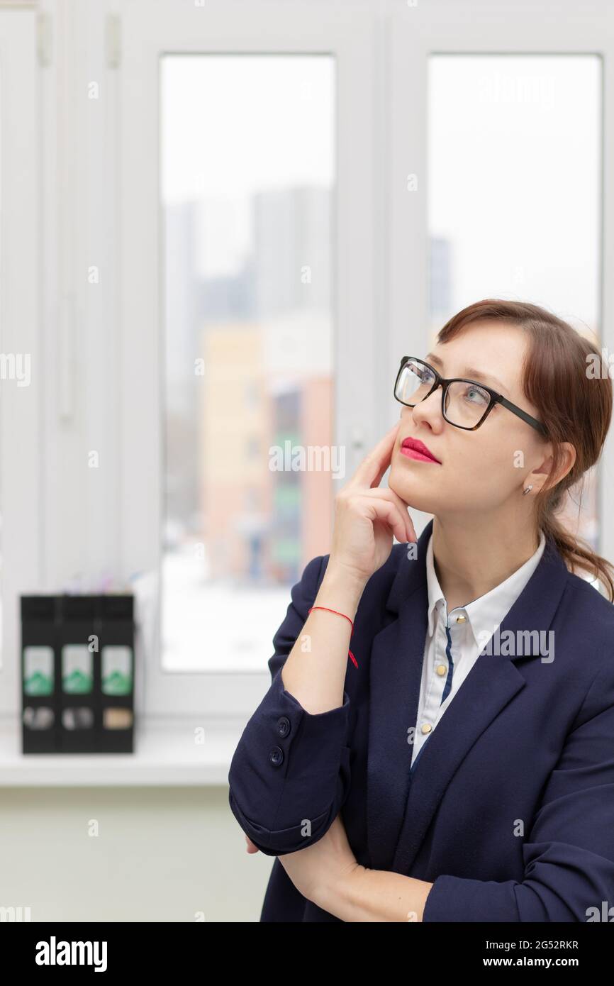 young strict business woman in a blue jacket and glasses is thinking at ...
