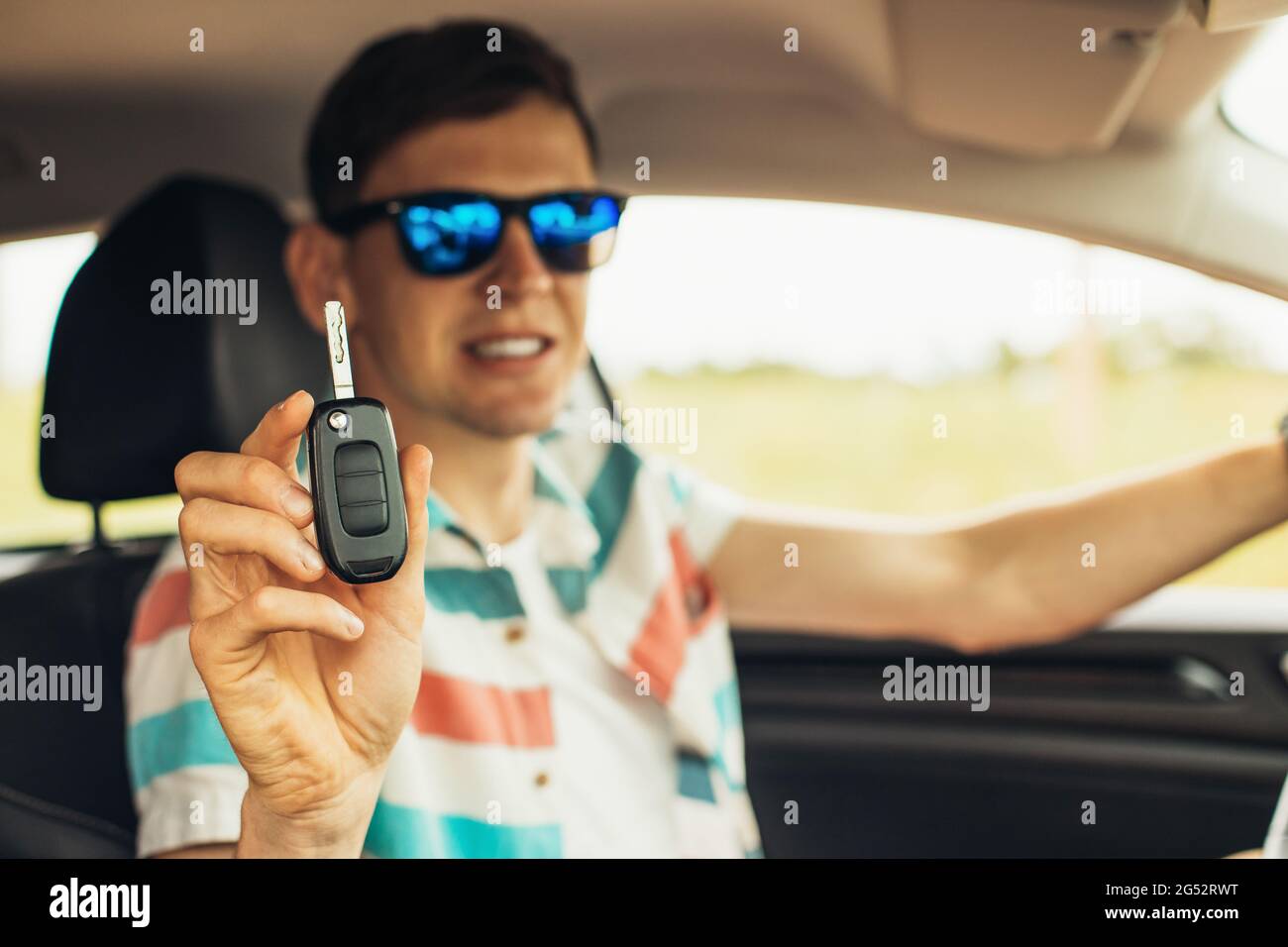 Happy young man with car key sitting in modern auto outdoors on a sunny ...