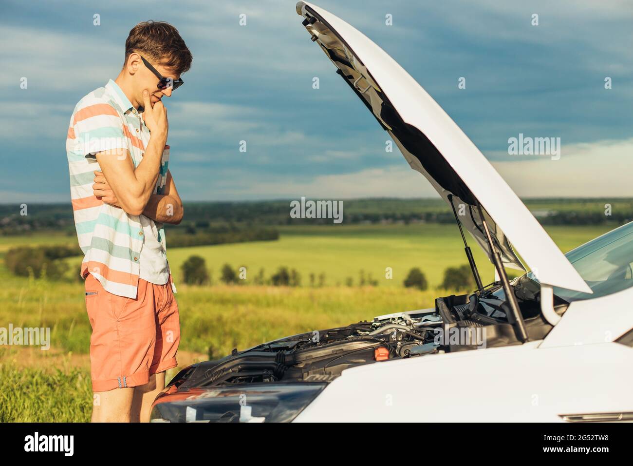 Breakdown of the car. Concentrated young man holding on to the hood of ...