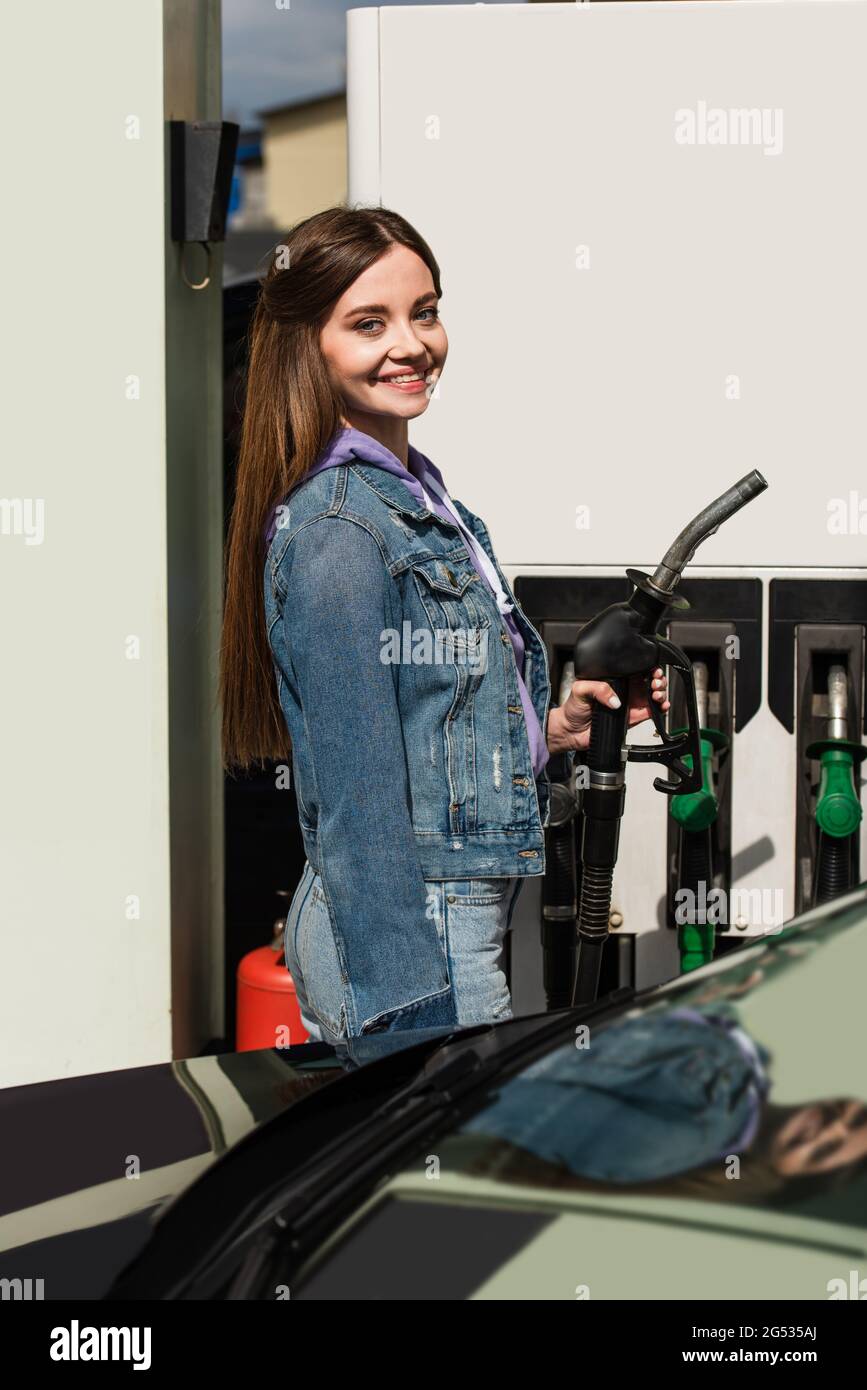 happy young woman smiling at camera while holding fuel pistol on ...