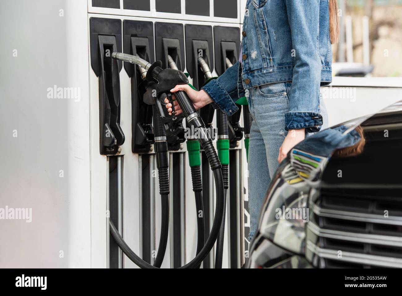 partial view of woman in denim clothes near fuel pistols and blurred ...