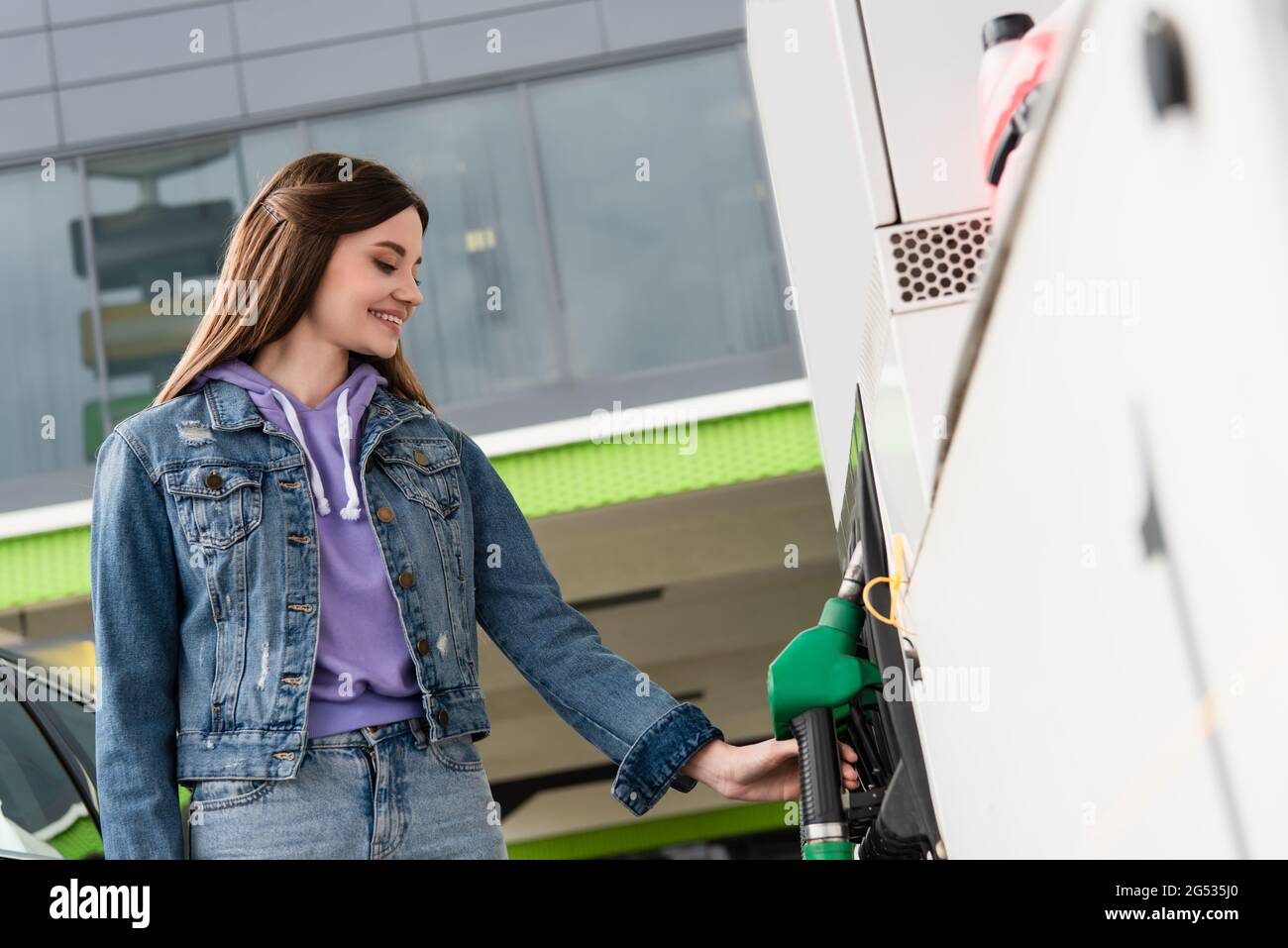 smiling woman in denim jacket taking fuel pistol on gas station Stock ...