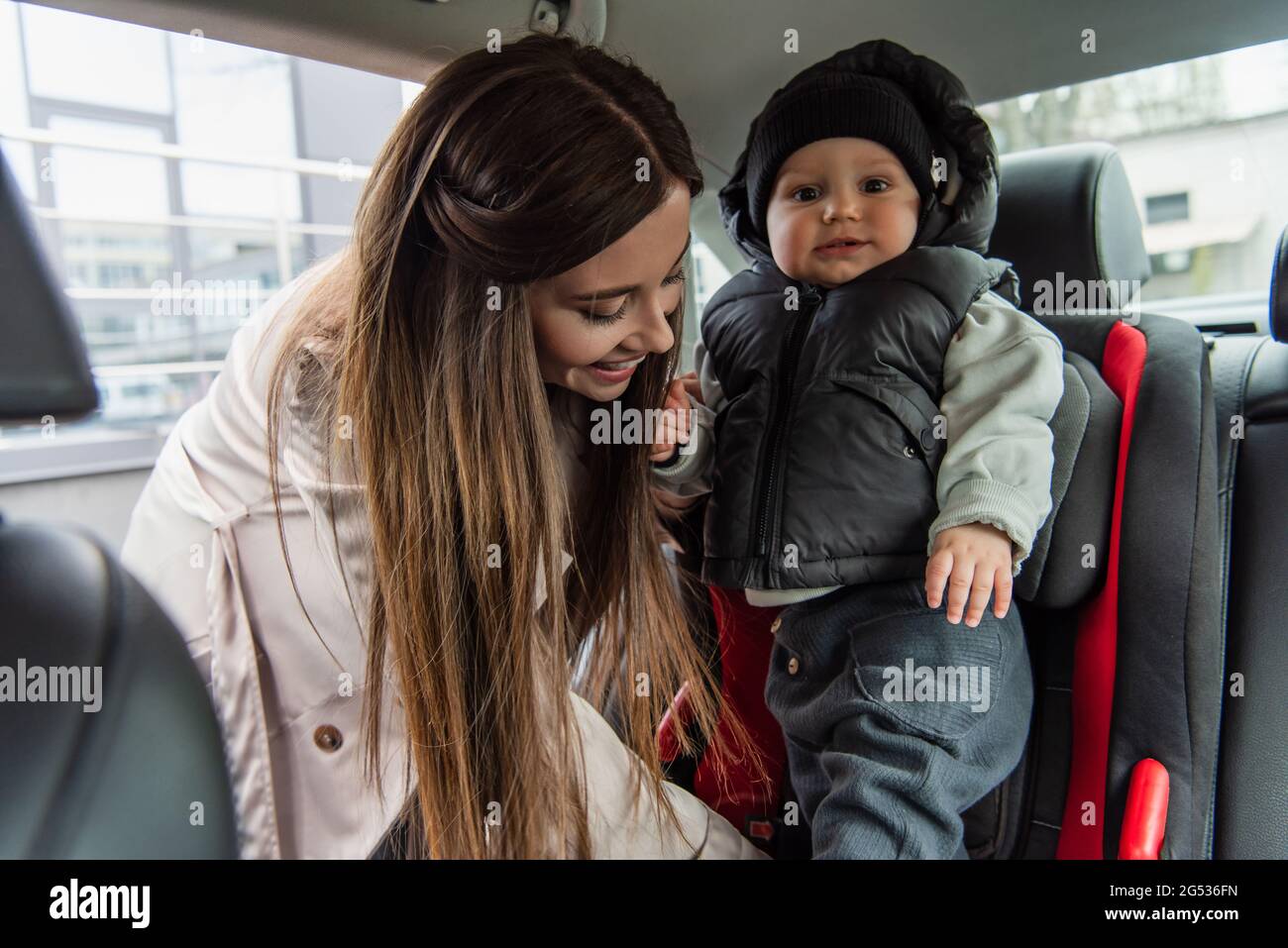 smiling woman putting little son into baby car chair Stock Photo - Alamy