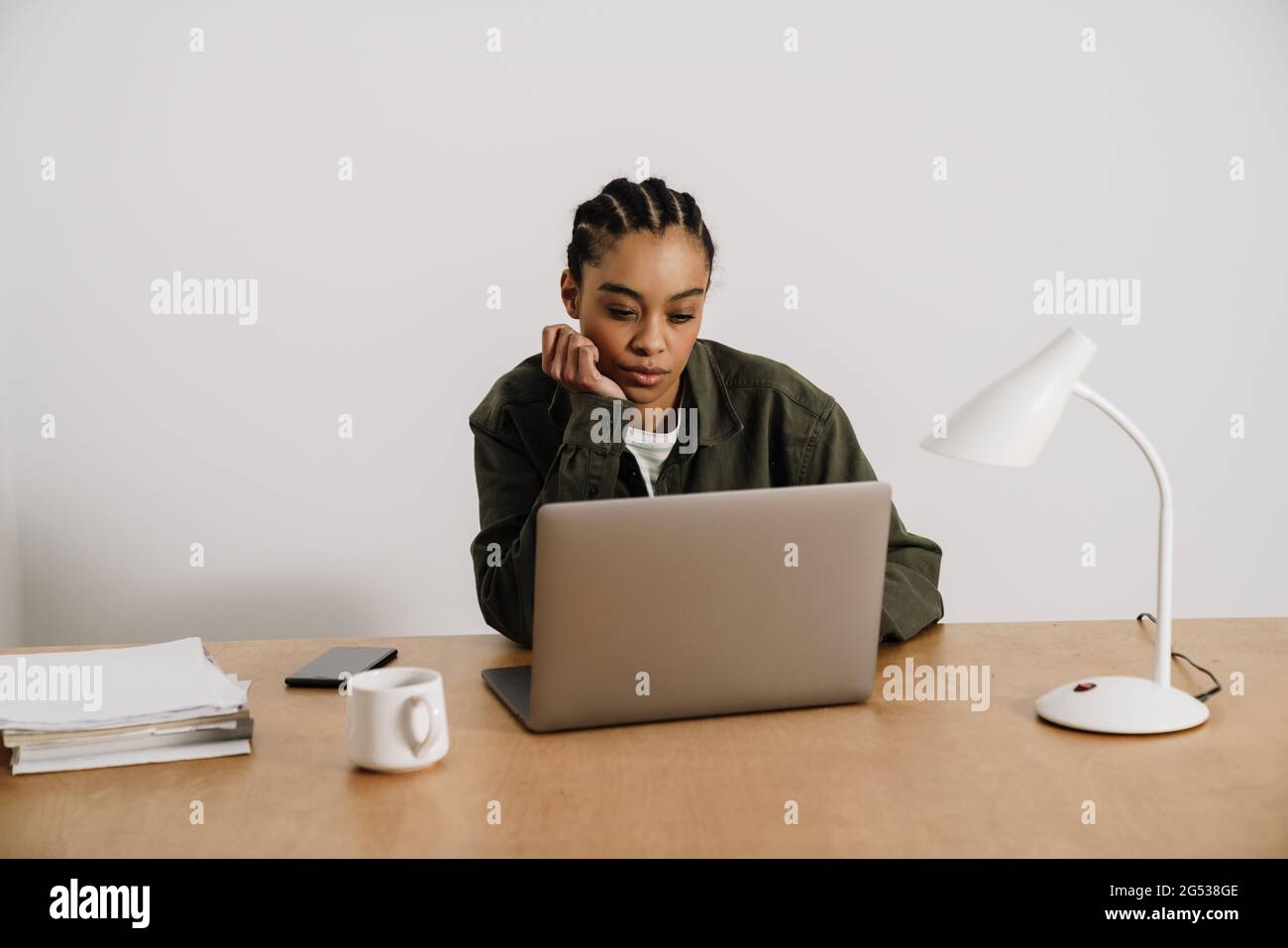 Black young woman working with laptop while sitting at table in office ...
