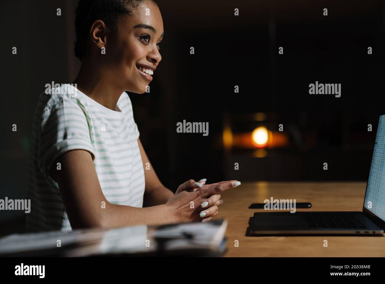 Black smiling woman working with laptop while sitting at table in ...