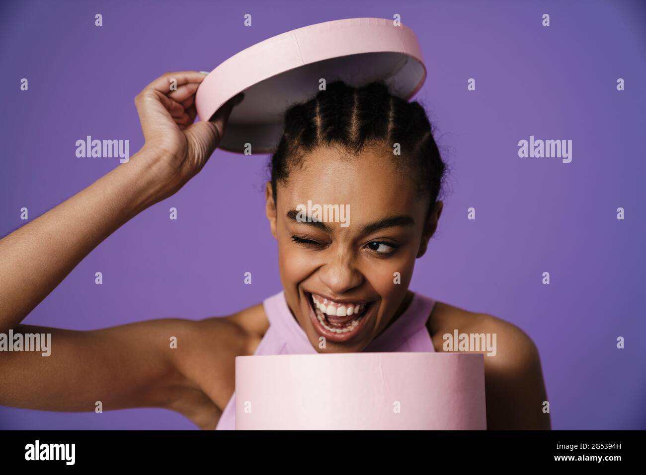 Joyful black woman winking while making fun gift box isolated over ...