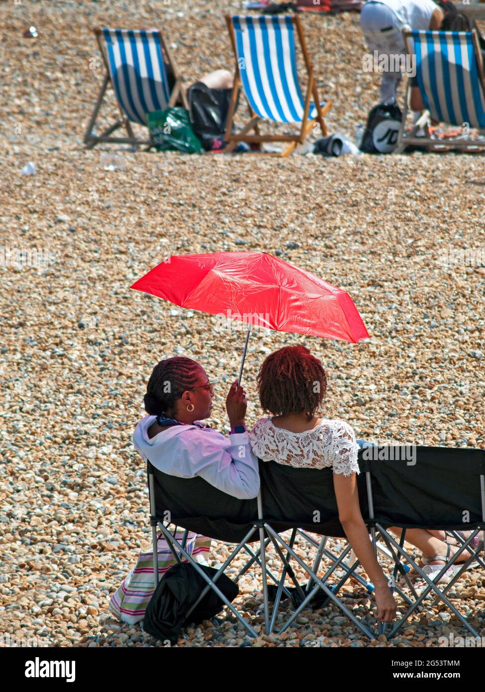 Seeking shade from a red umbrella on the beach at Brighton Stock Photo ...