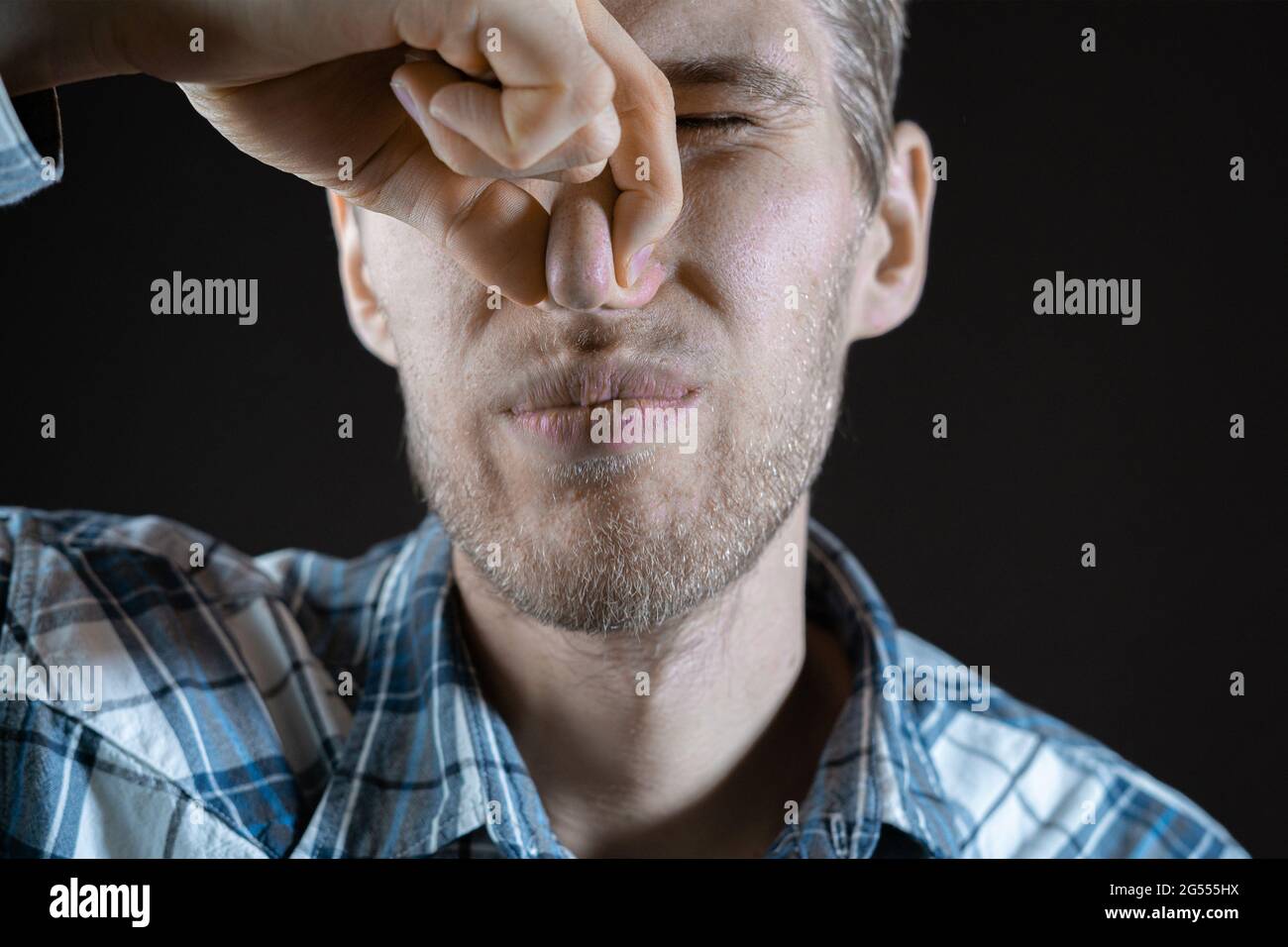 man close his nose on dark background, stink smell, fells disgusting ...