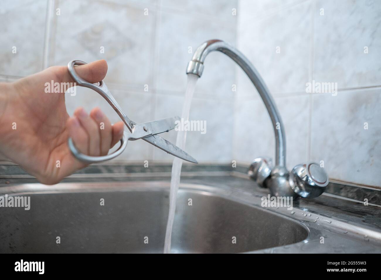 stop wasting the pure water, hand with scissors cut the water stream ...