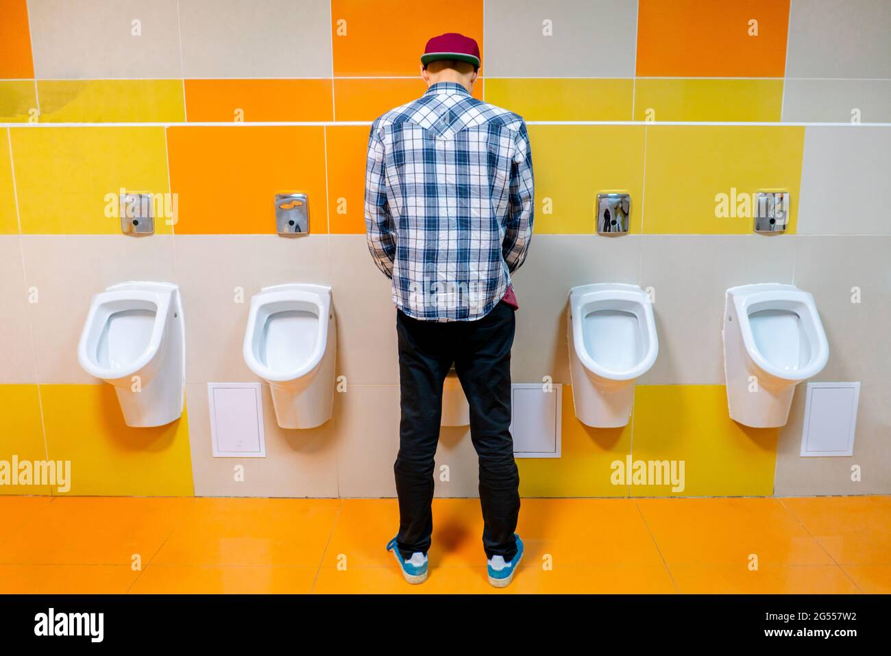 young man in the public toilet, standing next to the urinal in the ...
