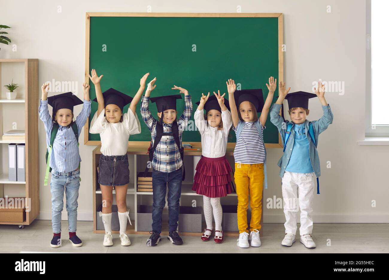 Group of happy school children in academic hats standing in front of ...