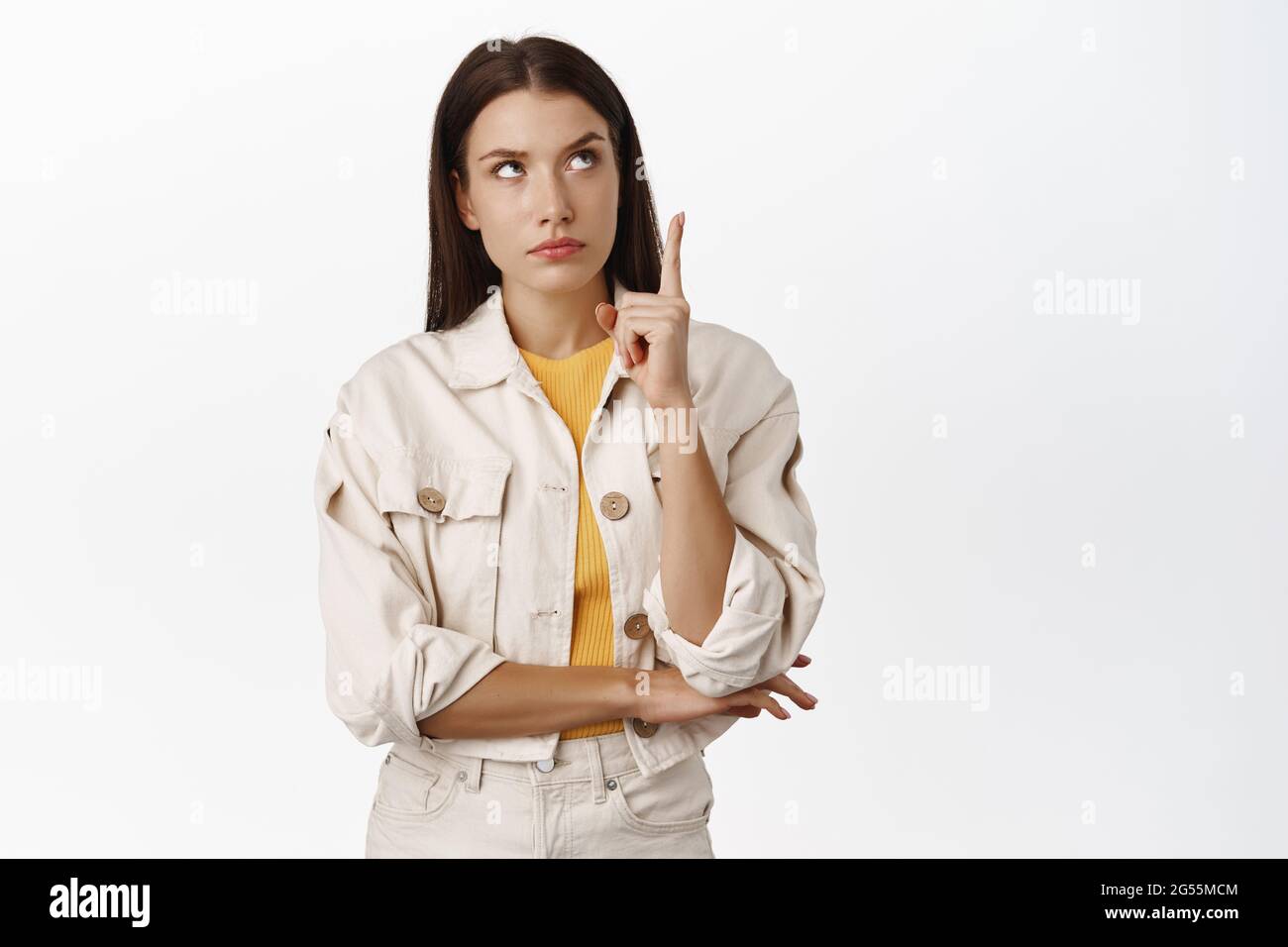 Thoughtful woman in trendy outfit, pointing finger up, looking with ...
