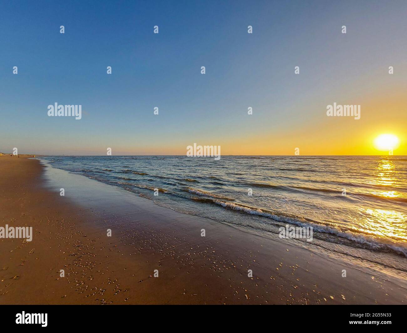 sun sinks into the sea on the beach of Katwijk with colorful sky in the ...