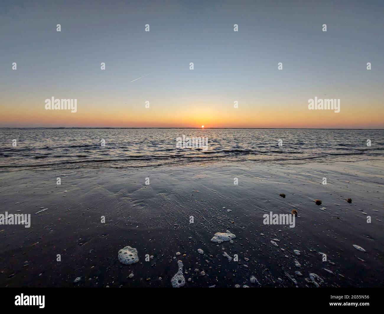 sun sinks into the sea on the beach of Katwijk with colorful sky in the ...
