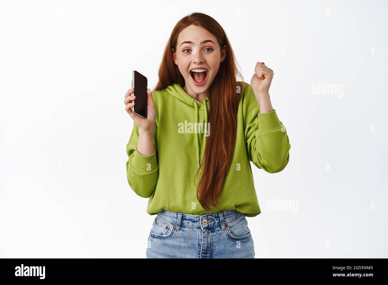 Excited winning ginger girl celebrating, winning money on mobile phone ...
