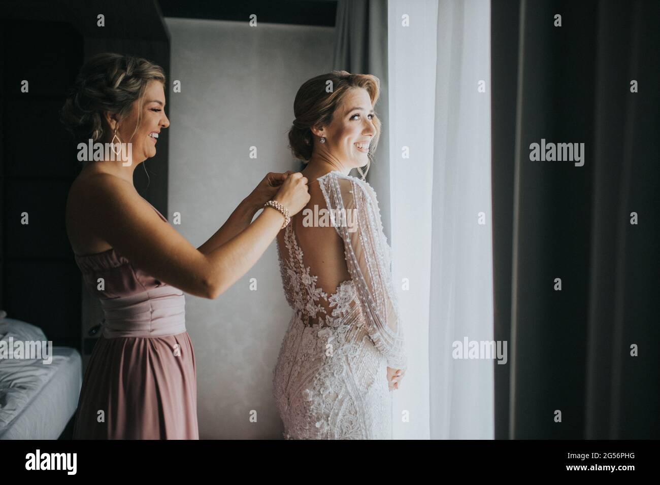 Bridesmaid helping the bride to get dressed for the wedding ceremony ...