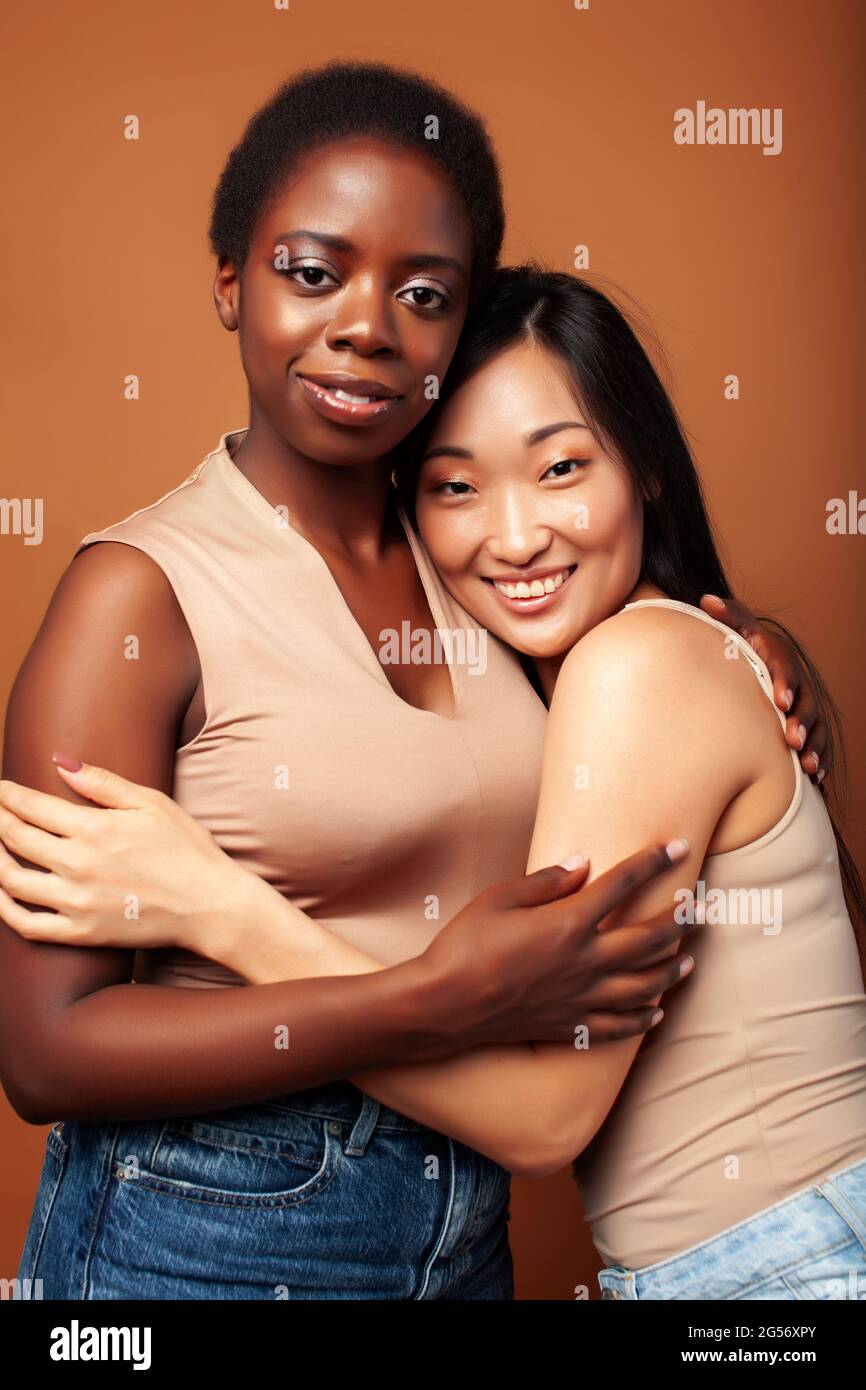 young pretty asian, afro woman posing cheerful together on brown ...