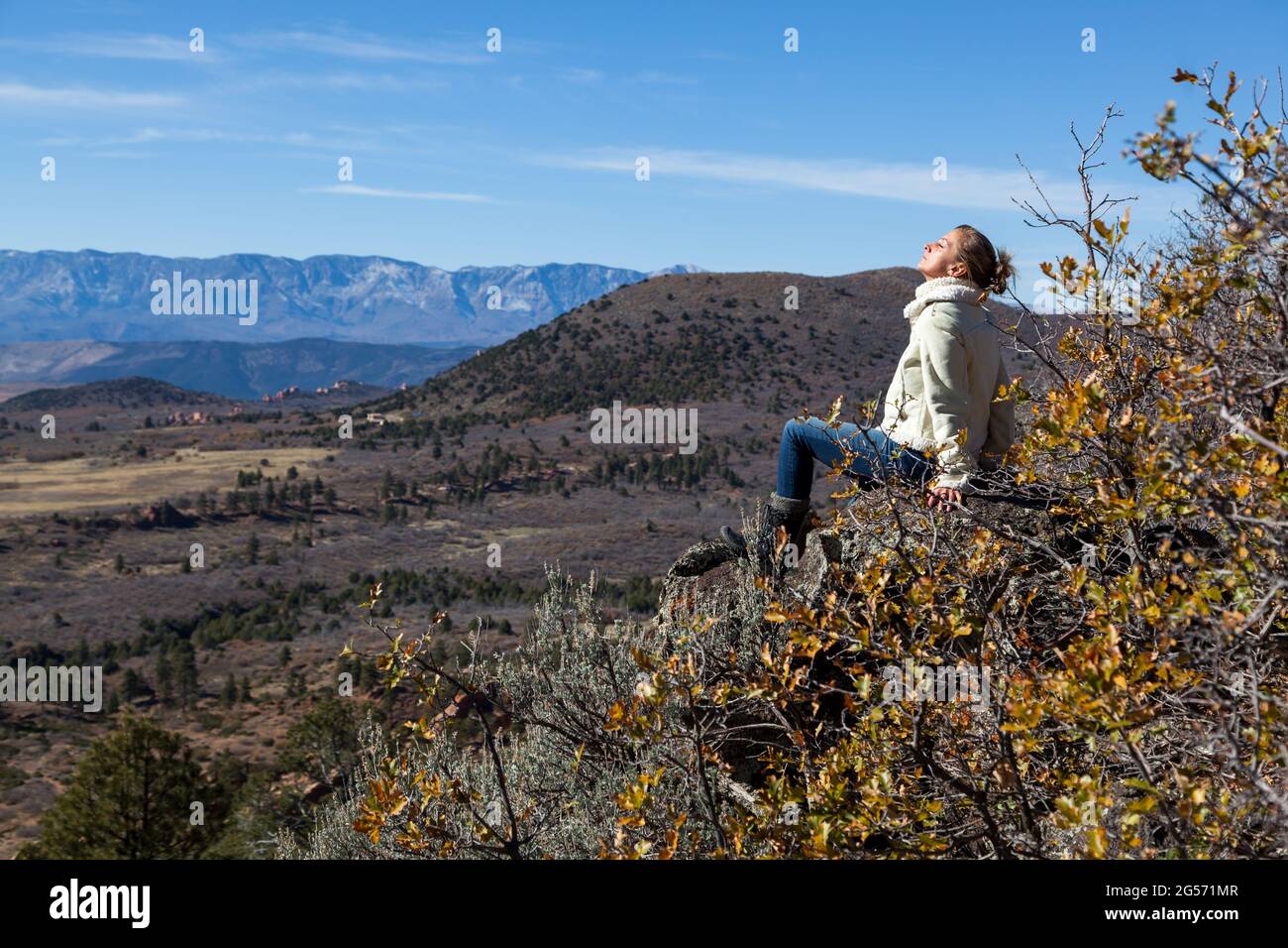 A woman enjoying the fall sunshine high up on a rock overlooking a ...