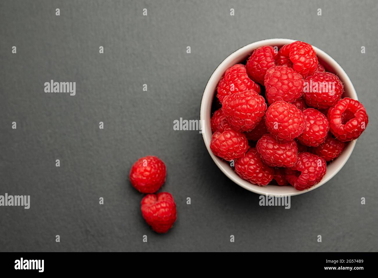 Fresh juicy raspberries in a small black plate. Bright red crimson ...