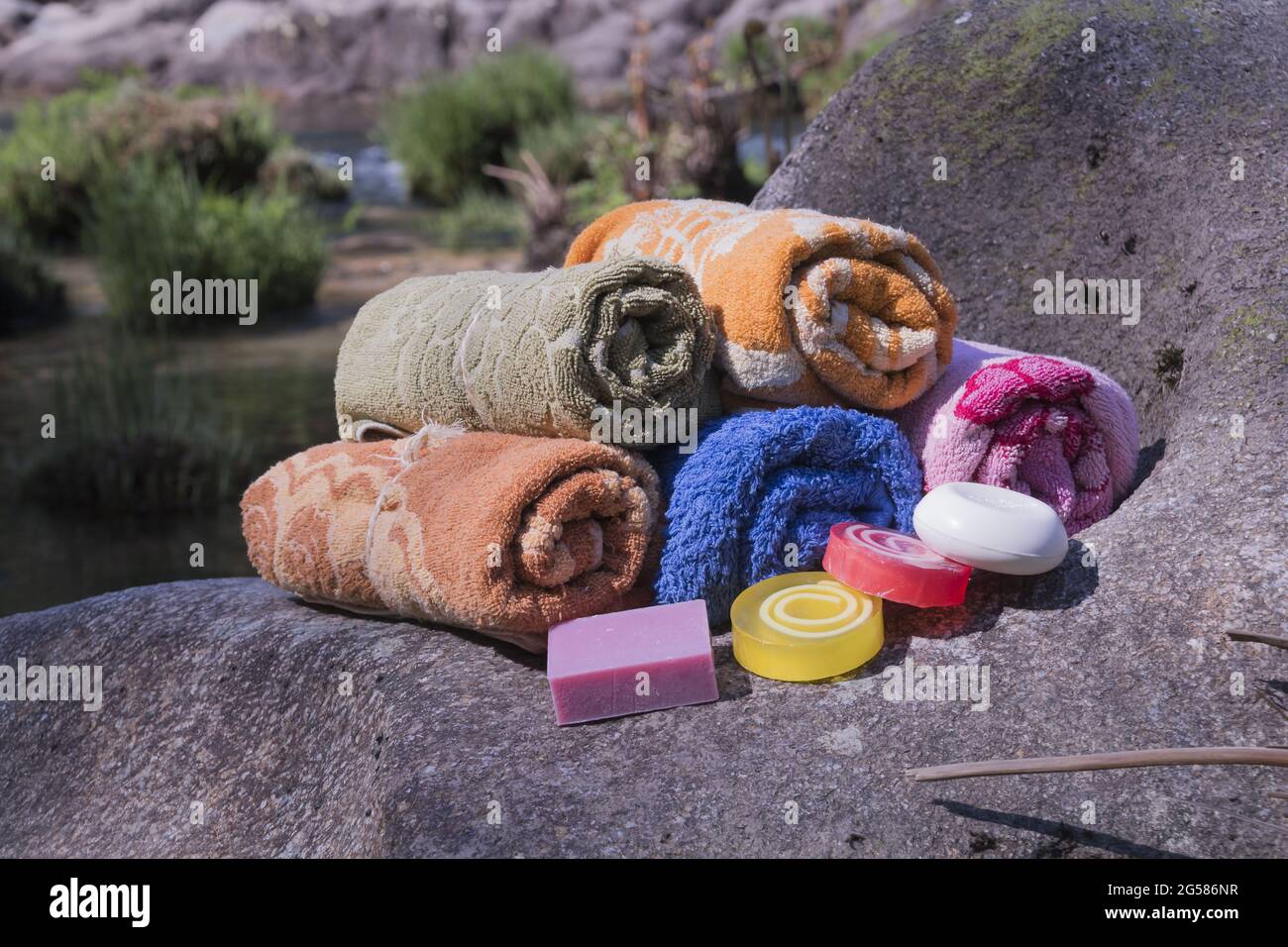Pile of rolled colorful towels and decorative soaps on a rock surface ...