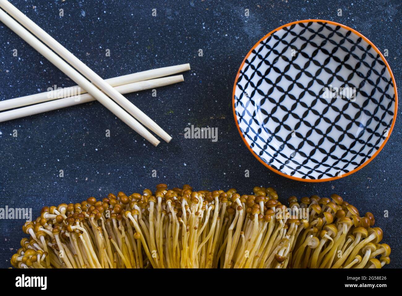 Top view of golden Asian Enoki mushrooms next to a bowl and chopsticks ...