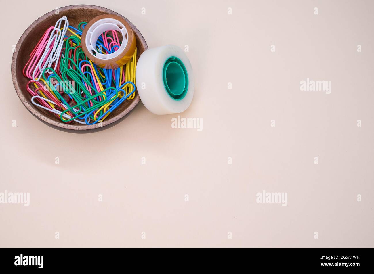 Top view of colorful paper clips and adhesive tapes in a wooden bowl ...