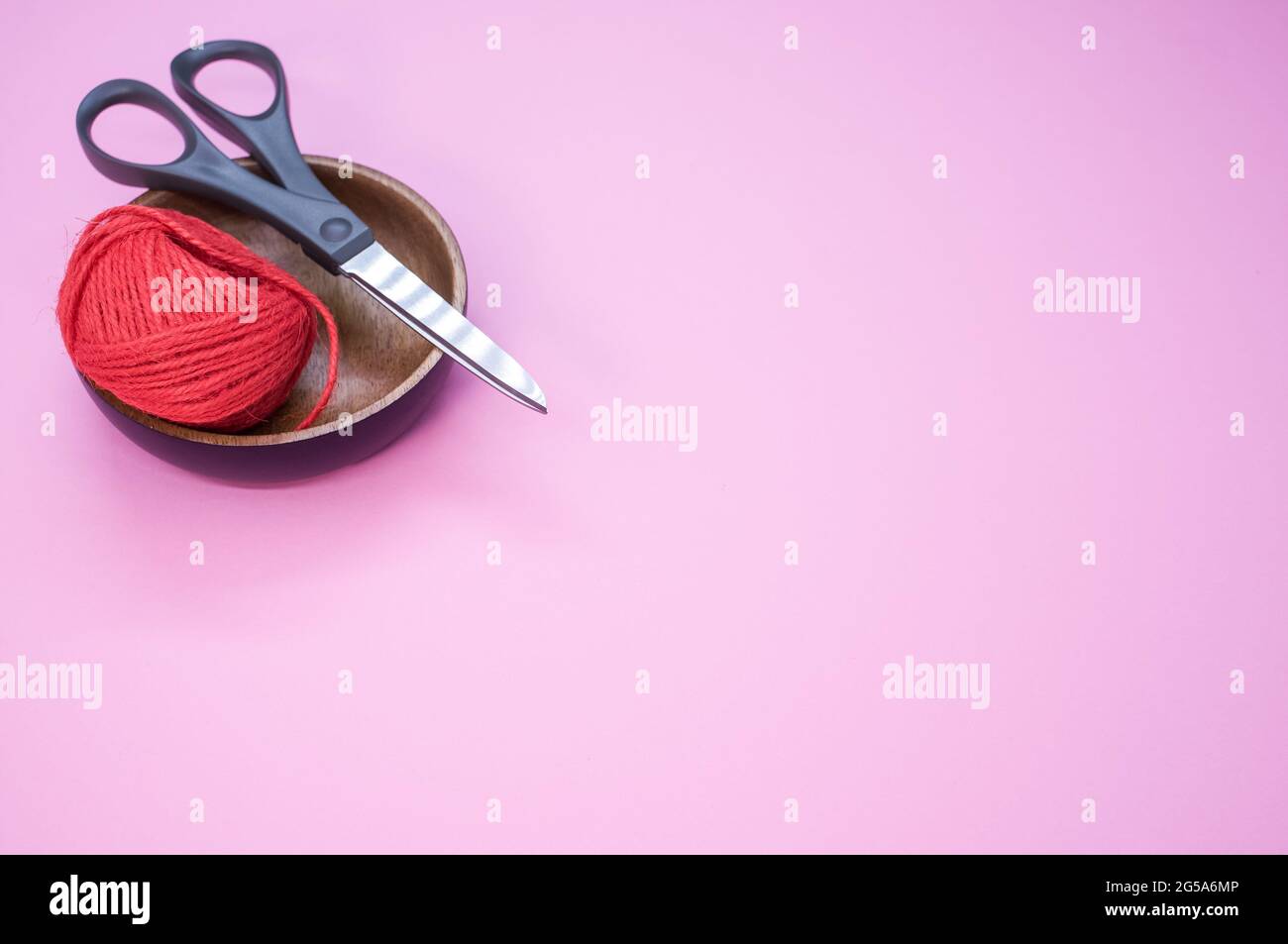 Closeup shot of red yarn for knitting and scissors in a wooden bowl on ...