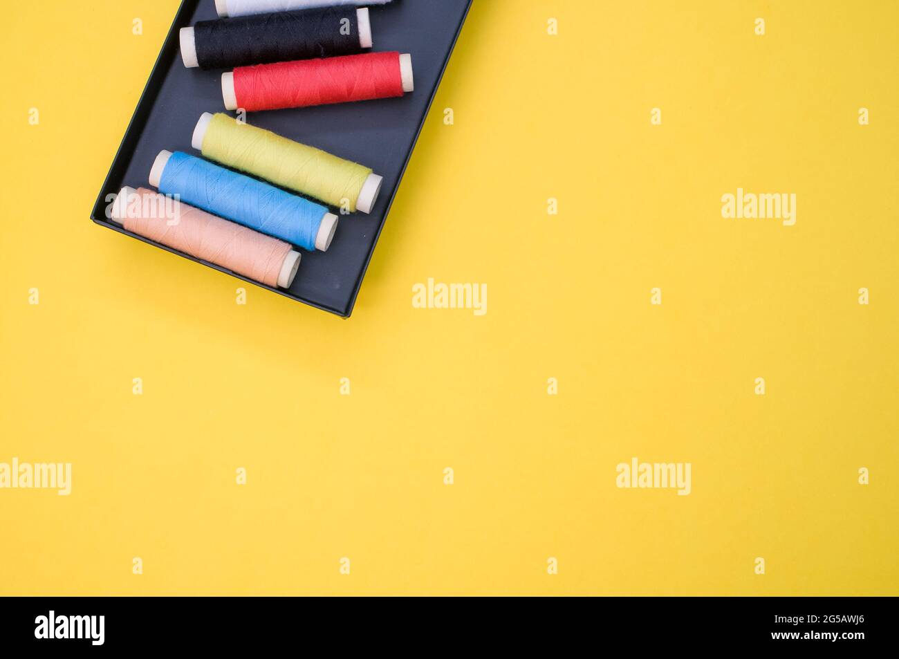 Pack of colorful sewing threads on yellow background with a copy space ...