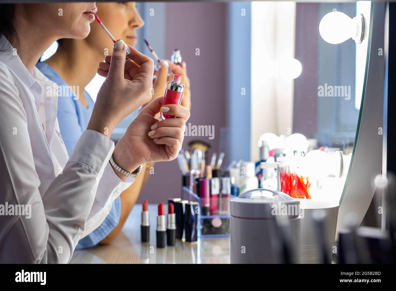 Closeup makeup artist teaching woman client applying lip gloss at ...