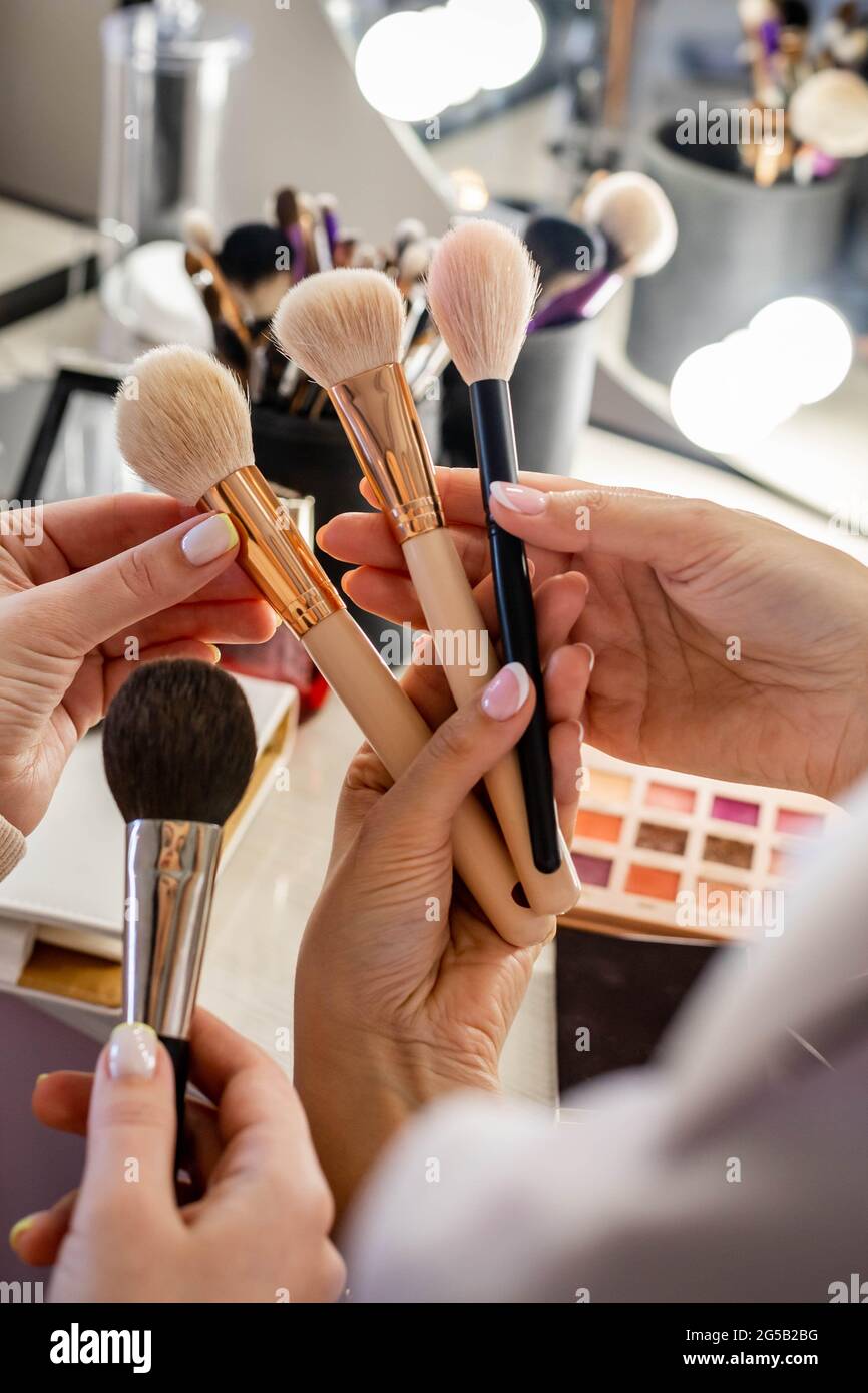 Close up hands of female makeup artist studying client choosing brush ...