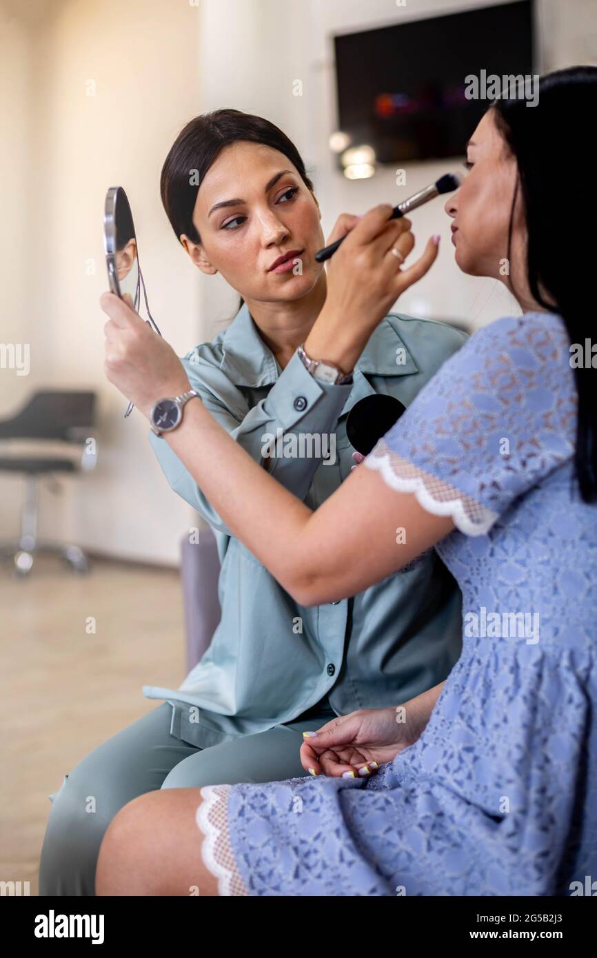Professional makeup artist teaching female client applying blush on ...