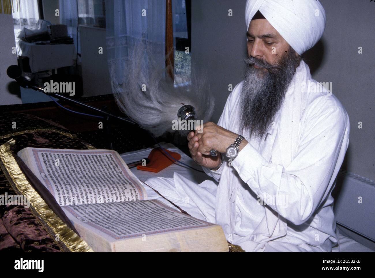 Sikh elder reading from the holy Guru Granth Sahib during worship in a ...