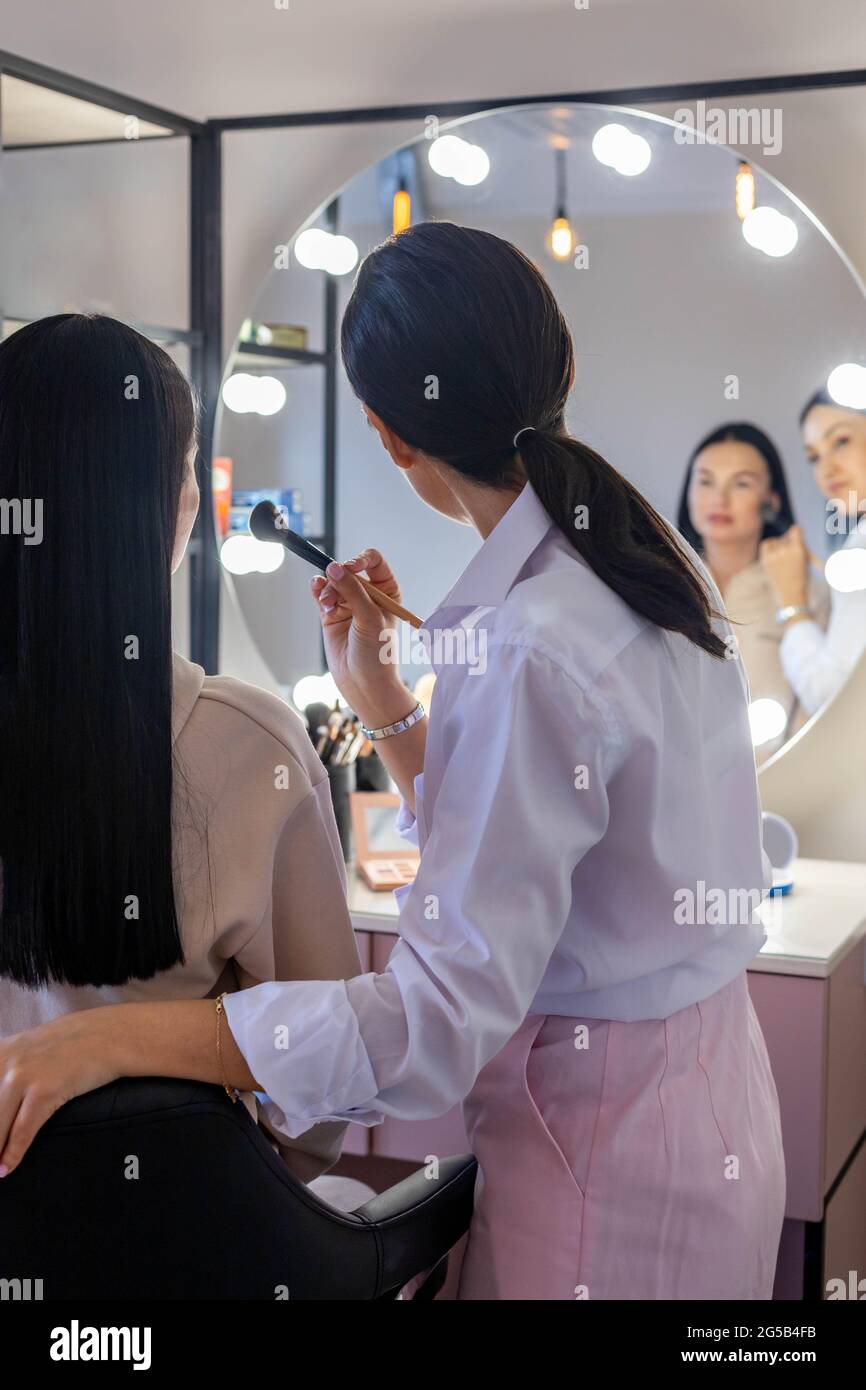 Professional makeup artist teaching female client applying blush on ...